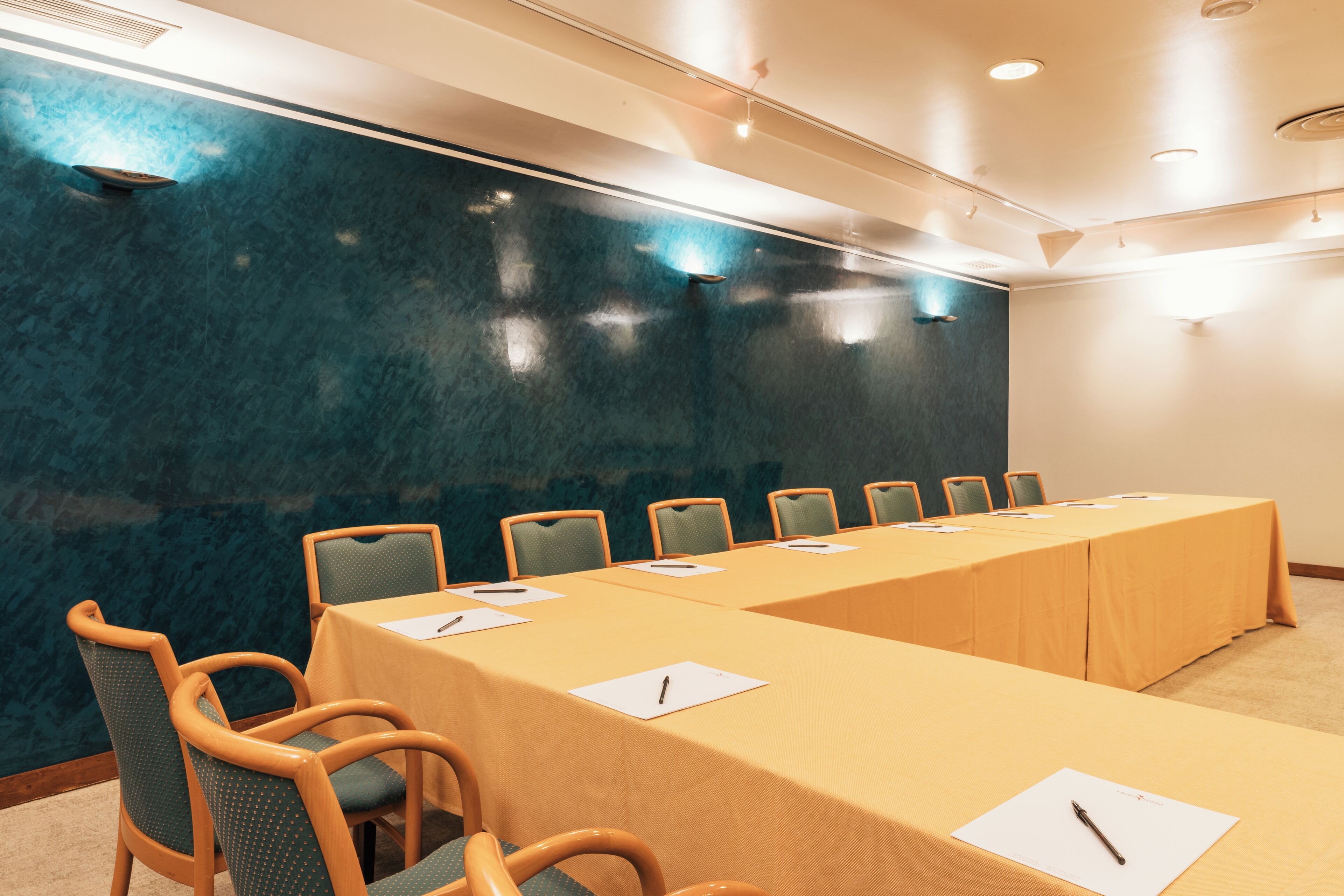 Uma sala de conferências com uma mesa comprida, cadeiras e uma parede azul com textura.