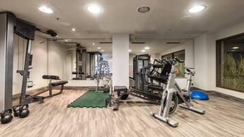 Uma academia com diversos equipamentos de exercício, um tapete verde e uma bicicleta ergométrica.