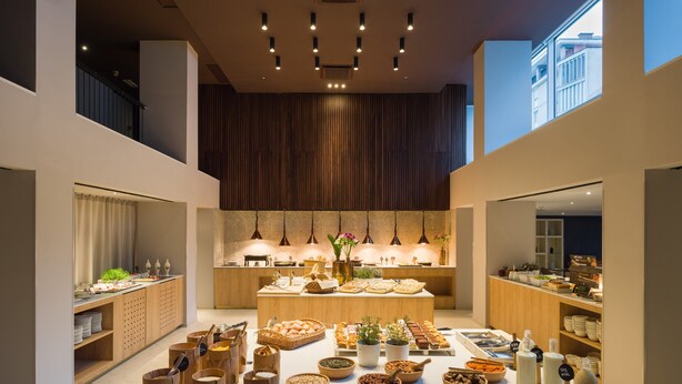 Um hall de hotel moderno com uma área de buffet central que oferece diversas opções de comida e um balcão de recepção de madeira.