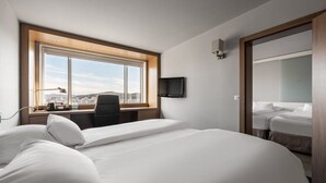 Quarto de hotel com uma cama grande, uma mesa com cadeira, uma TV fixada na parede e uma janela com vista para a cidade.