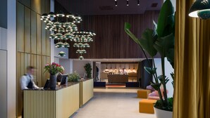 Uma área de recepção moderna com um balcão de madeira, várias luminárias pendentes e um espaço de estar com almofadas amarelas.