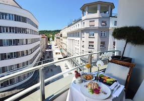 Varanda com mesa posta para o pequeno-almoço, com vista para uma rua da cidade, prédios e céu limpo.