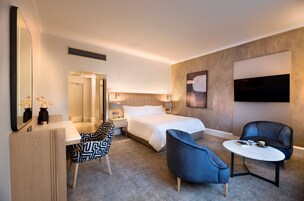 Quarto de hotel moderno com cama, escrivaninha com cadeira, mesa pequena e televisão.