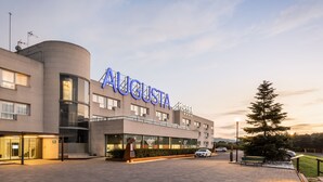 Um hotel moderno com uma placa grande com o nome 'Augusta Hotel', entrada bem iluminada e área de estacionamento.
