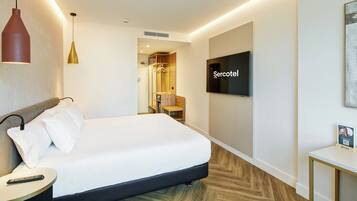 Quarto de hotel moderno com uma cama, uma televisão, uma mesinha e uma cadeira.