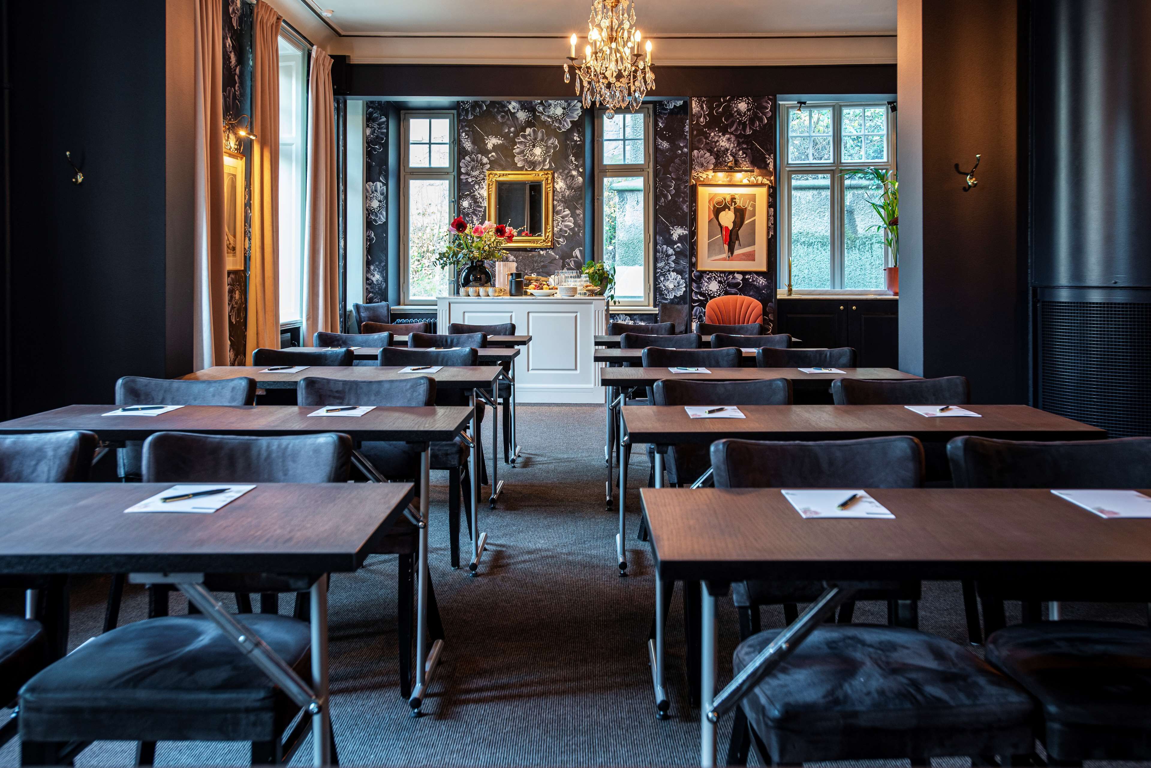 Um restaurante com disposição em longa mesa, um candelabro e um design floral na parede.