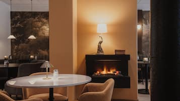 Um quarto acolhedor com uma mesa redonda, quatro cadeiras, lareira acesa e uma luminária na parede.