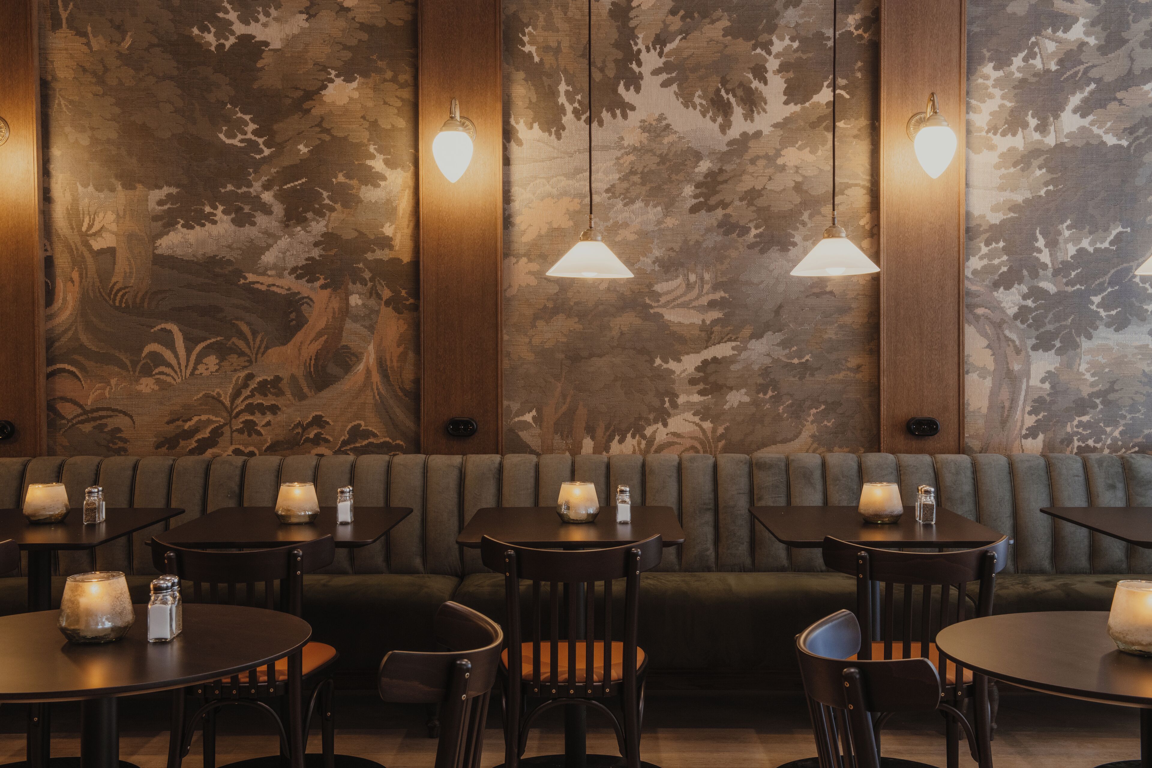 Interior de restaurante com painéis de madeira, assentos acolchoados e iluminação pendente. As mesas estão postas com velas.