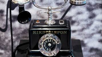 Um telefone RIKSTELEFON antigo com discador rotativo, um fio e uma base de metal.