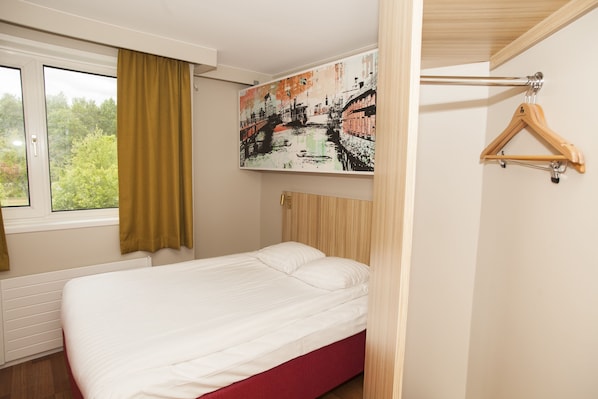 Cama bem arrumada em quarto com janela, um quadro na parede e um cabide de madeira.