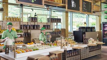 Um café com estação de autoatendimento para bebidas, prateleiras com produtos embalados e uma máquina de café.