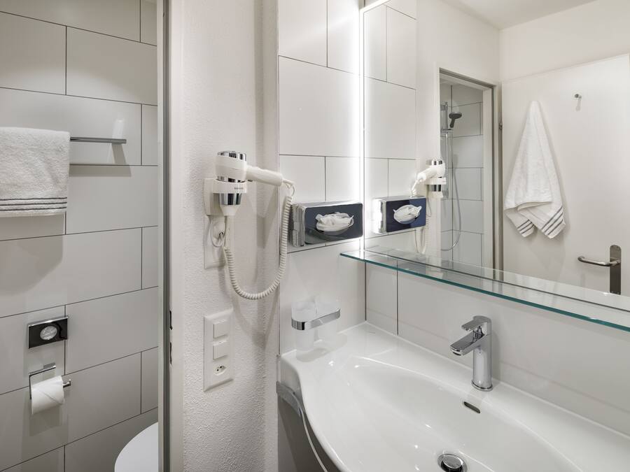 Uma casa de banho moderna com cabine de duche em vidro, lavatório branco e porta-toalhas.