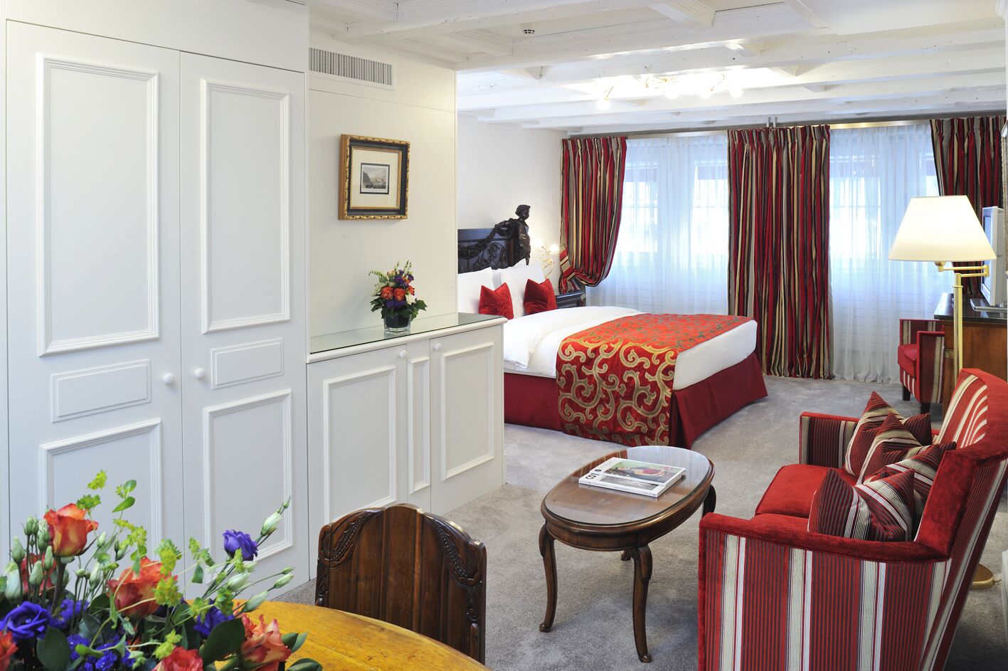 Quarto de hotel com cama, escrivaninha, cadeira, sofá e mesa de jantar.