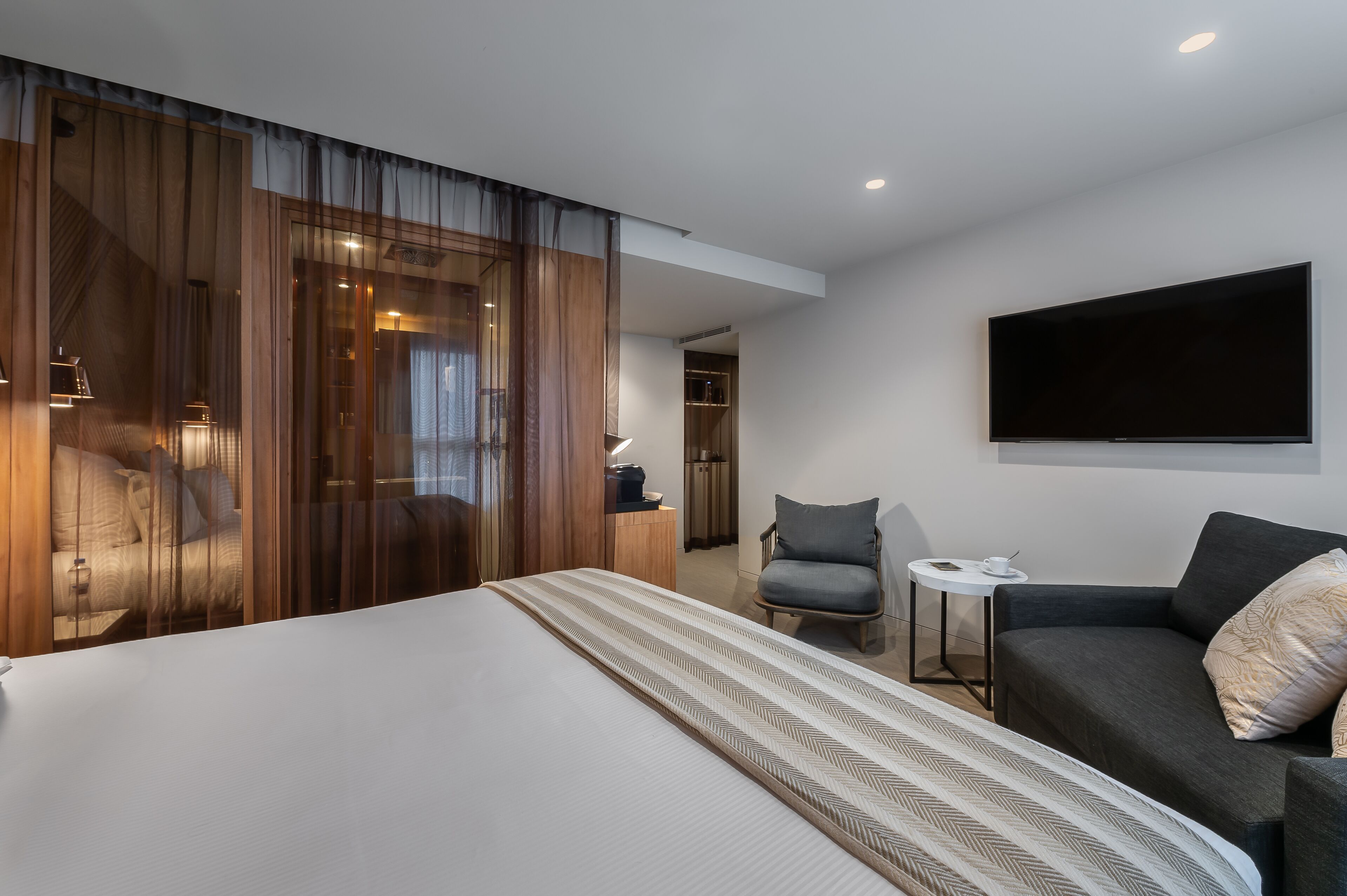Quarto de hotel moderno com uma cama grande, um sofá, televisão presa à parede e um closet espaçoso.