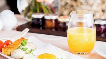 Mesa posta para o café da manhã com ovos, torradas e um copo de suco de laranja, com um vaso de flores ao fundo.