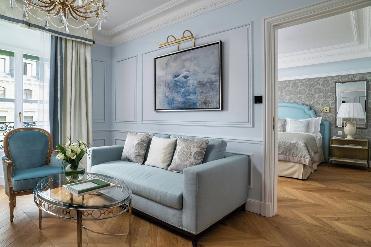 Quarto com um sofá azul claro, uma mesa de centro redonda de vidro, uma poltrona azul e um quadro abstrato grande na parede.