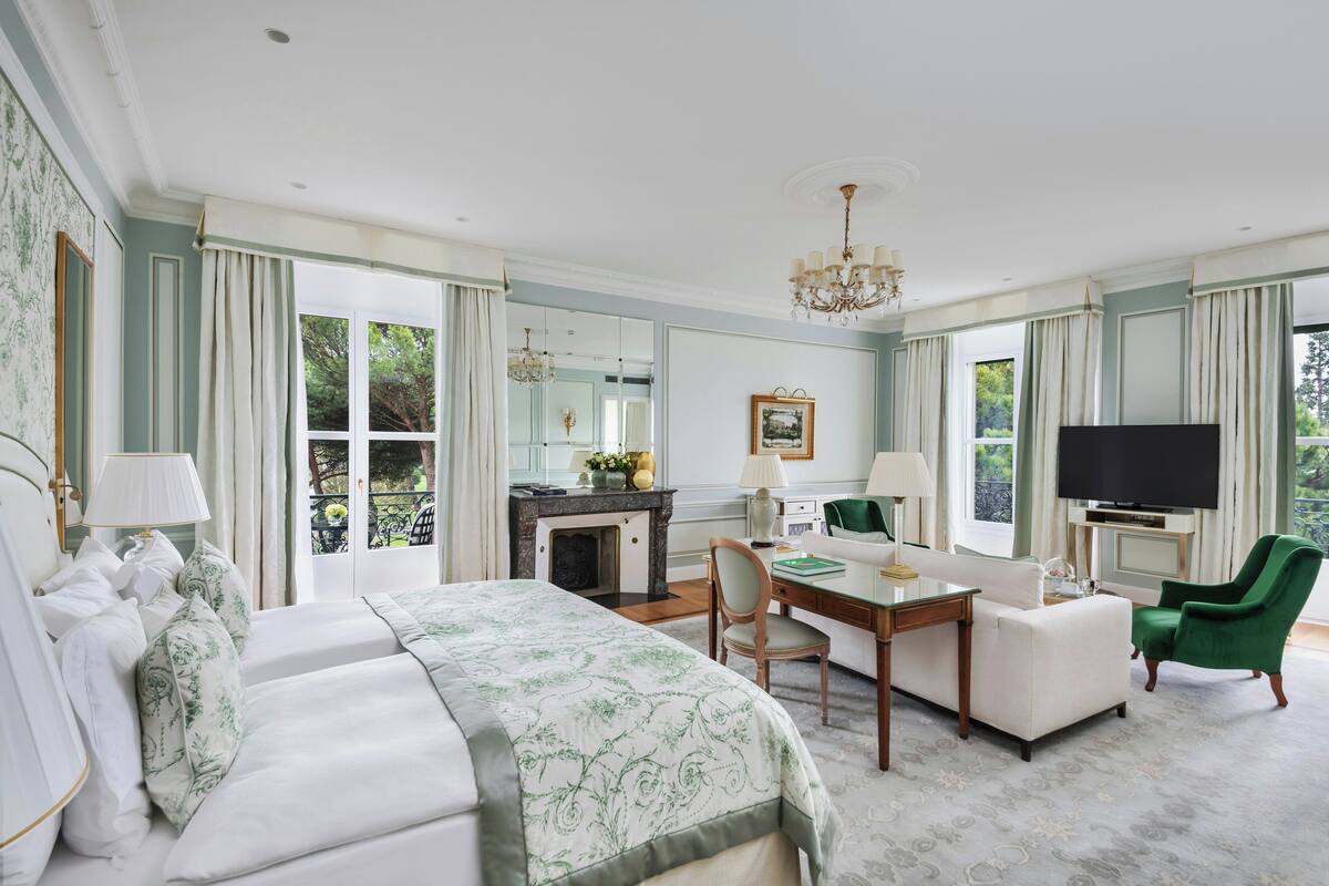 Quarto de hotel com uma cama, uma escrivaninha, uma televisão e uma poltrona verde.