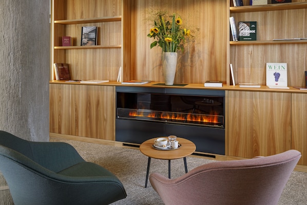 Uma sala de estar moderna com lareira, estantes de madeira com livros, um vaso com flores e duas cadeiras.