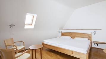 Quarto com cama de madeira, uma cadeira, uma mesinha, abajur e janela.