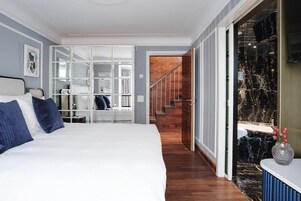 Quarto moderno com cama grande, closet espaçoso, escada de madeira e banheiro em mármore.