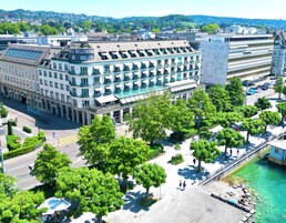 Um hotel grande com vários andares, um terraço no telhado bem visível e vista para a água.