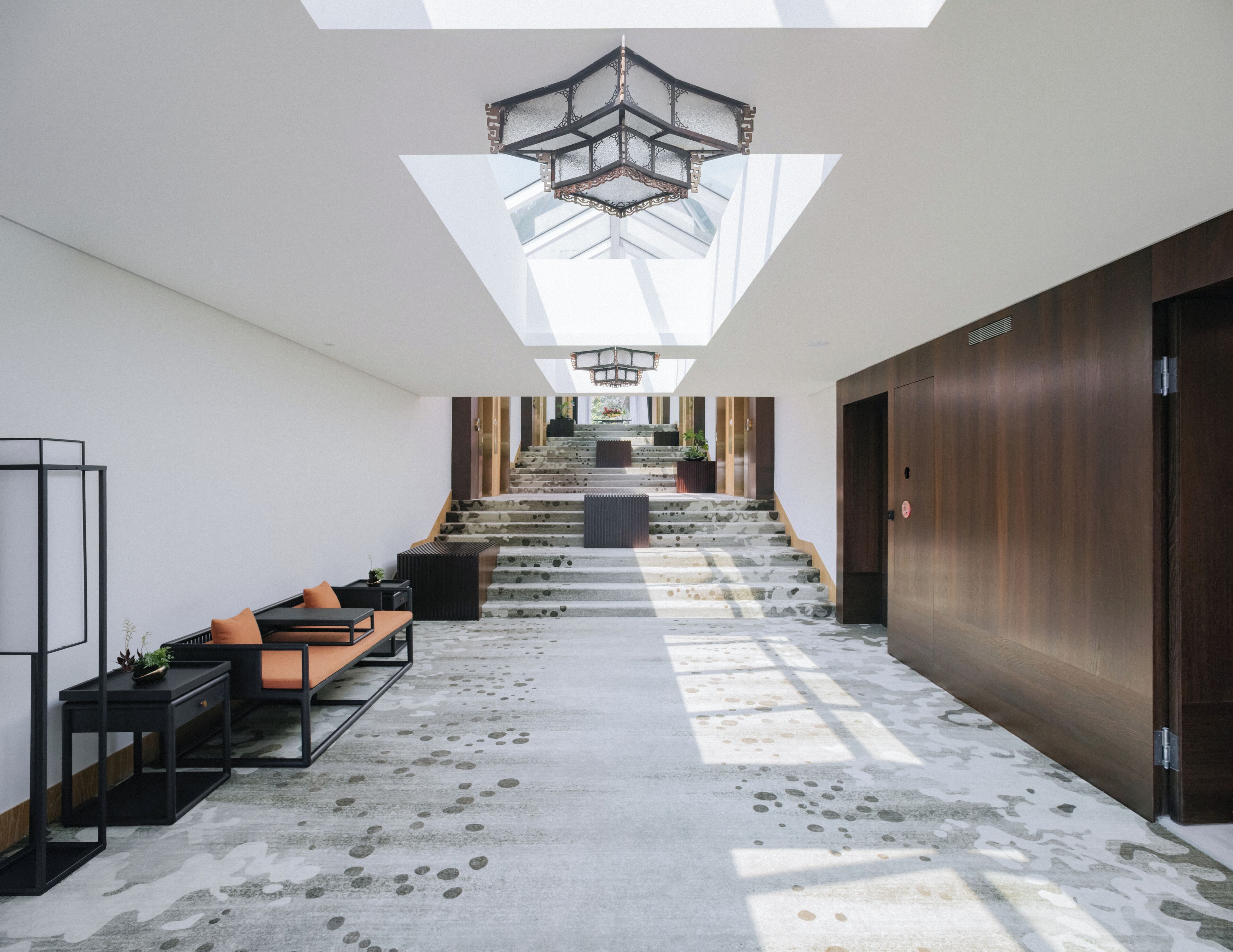 Interior moderno com escada que dá para um andar superior, área de estar com sofá e mesa de centro, e porta de madeira à direita.