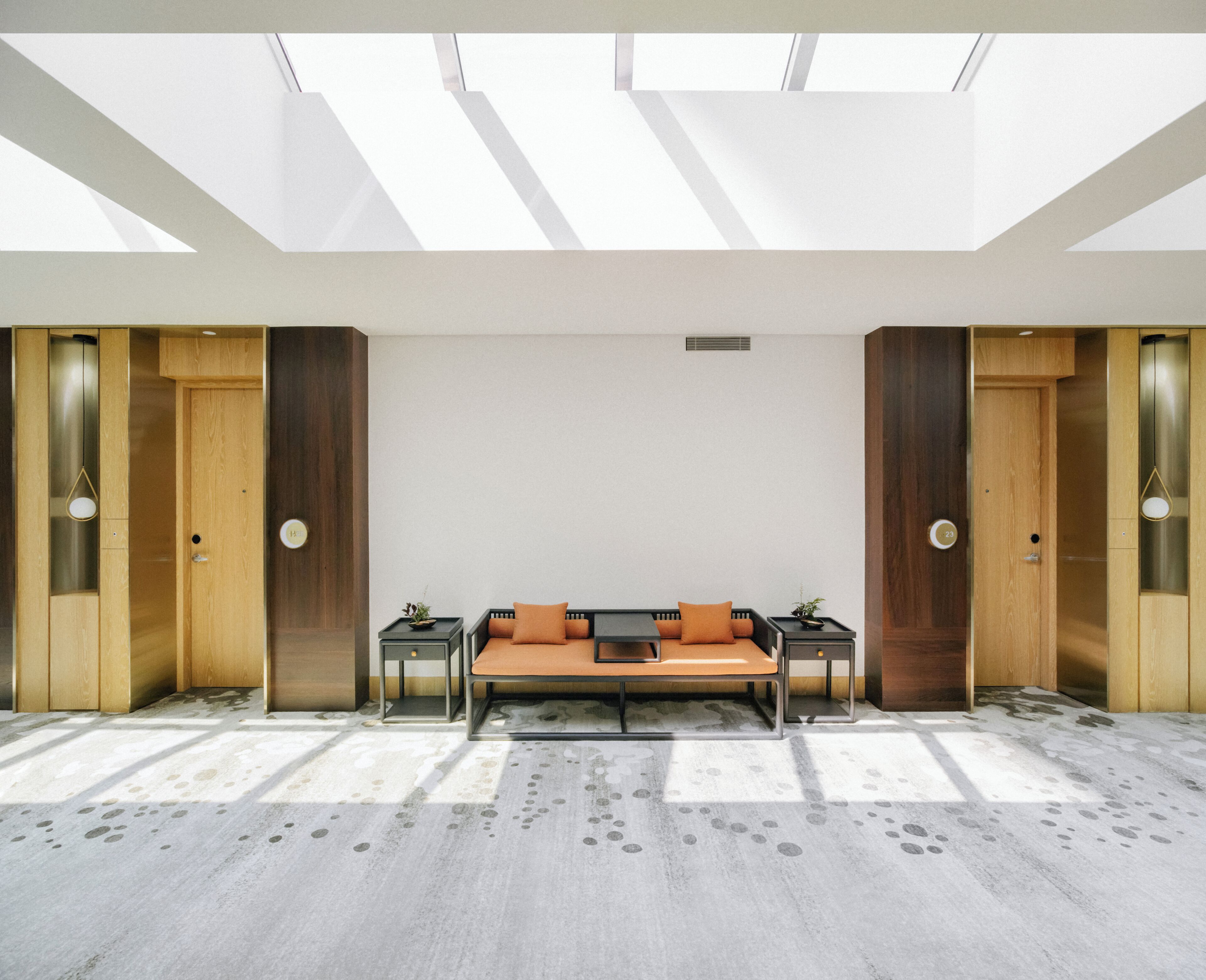 Um lobby moderno de hotel com área de estar central, lambris de madeira e um claraboia.