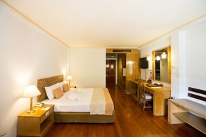 Quarto de hotel com cama, mesa de cabeceira com abajur, escrivaninha com cadeira e espelho.