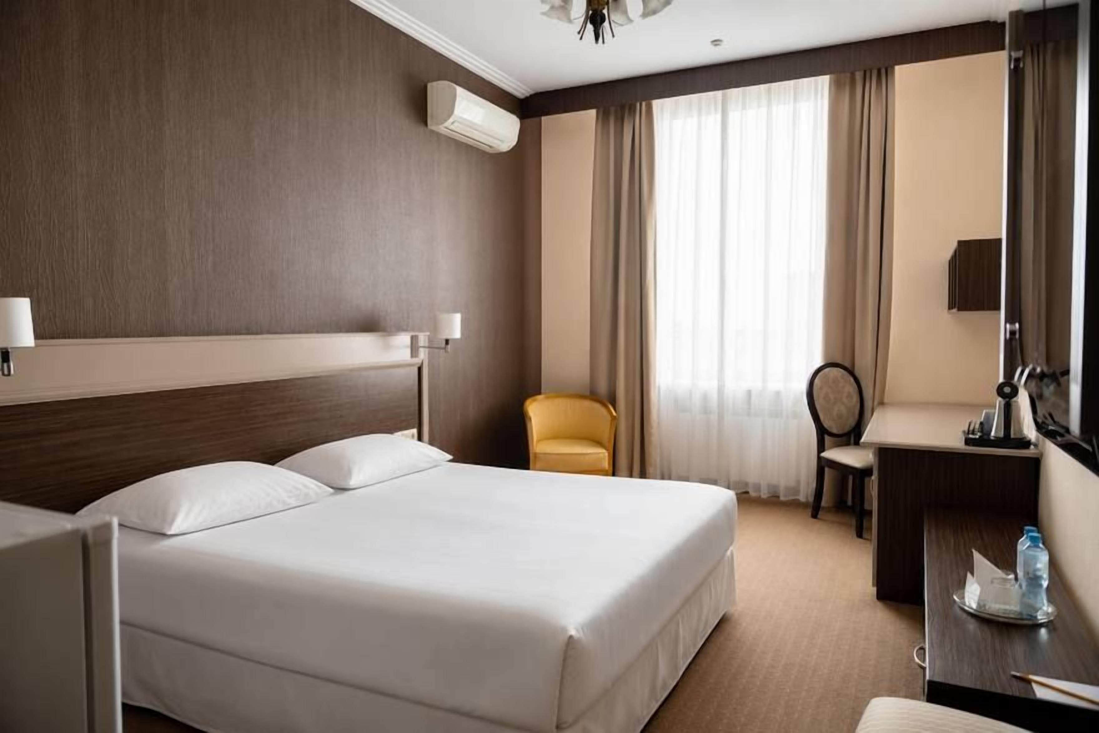 Quarto de hotel com uma cama grande, escrivaninha, cadeira e espelho.
