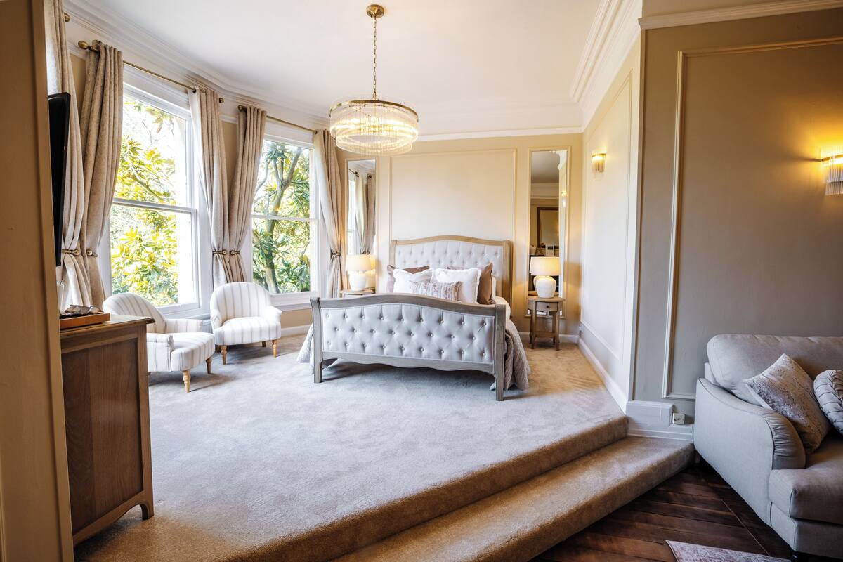 Quarto com cama grande, sofá, escrivaninha e janela com cortinas.