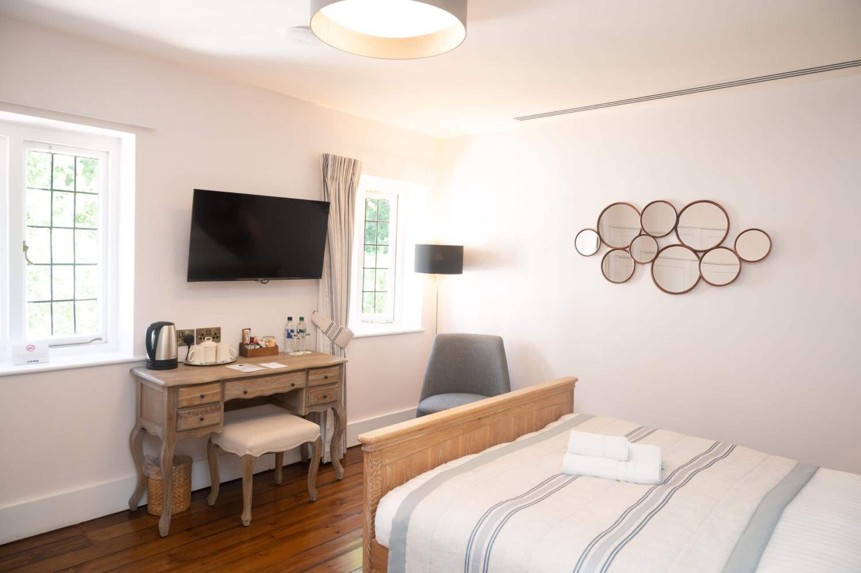 Quarto de hotel com escrivaninha de madeira, cadeira e cama com manta listrada.