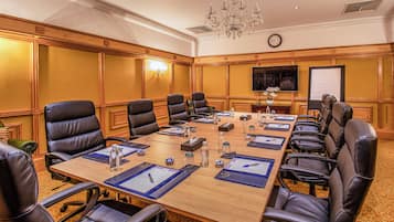 Uma sala de conferências com uma mesa comprida, várias cadeiras, um relógio e uma televisão na parede.