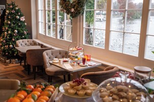 Uma sala de jantar acolhedora com uma árvore de Natal, mesa de buffet com diversos alimentos e vista para um rio através de amplas janelas.