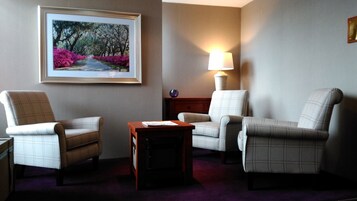 Um quarto com duas poltronas, uma mesinha, um abajur e um quadro emoldurado na parede.