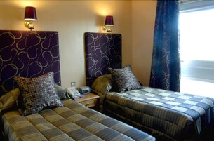 Quarto de hotel com duas camas, cada uma com cabeceiras estampadas e almofadas a combinar. Há abajures e um telefone na mesa de cabeceira.