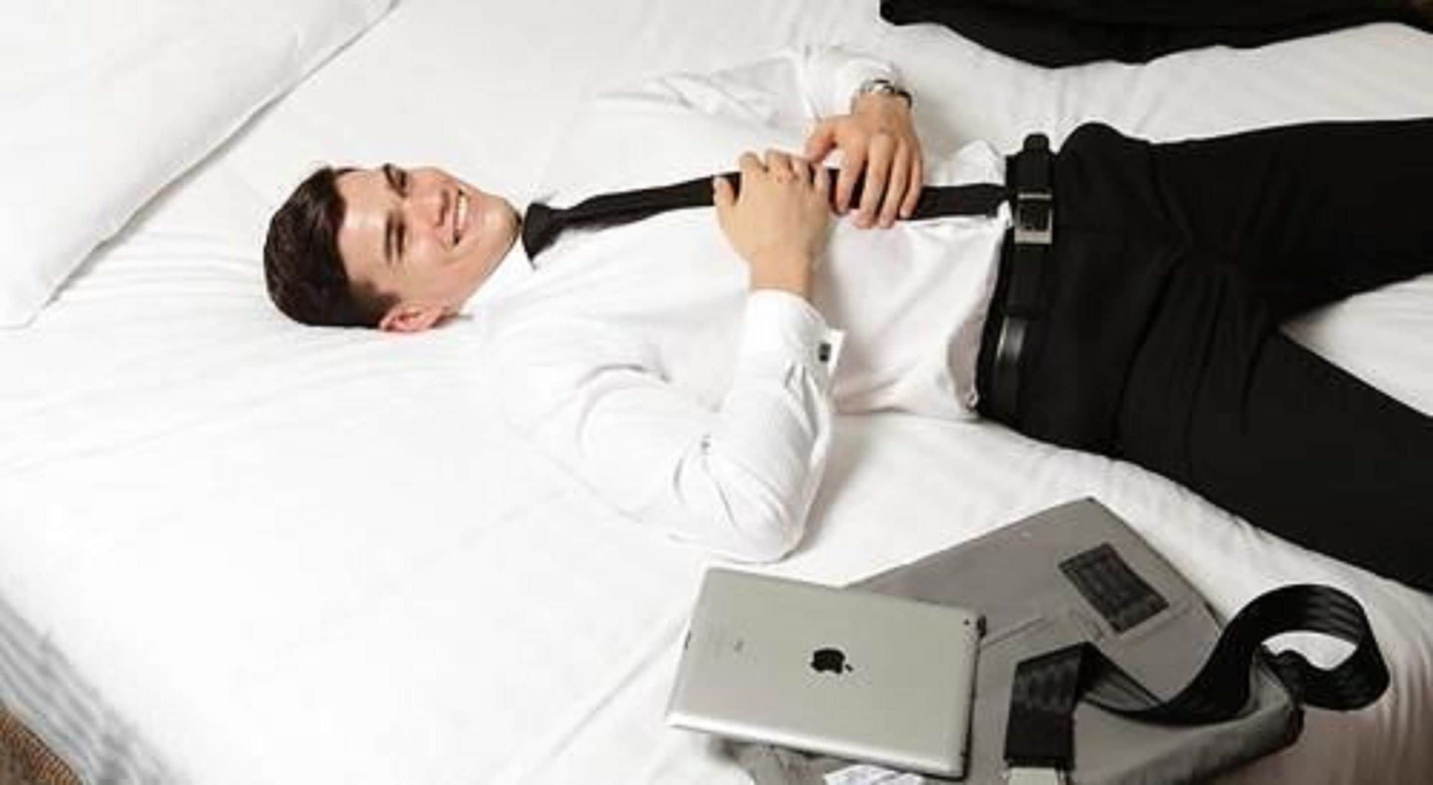 Uma pessoa deitada na cama com um laptop e um objeto preto ao lado.