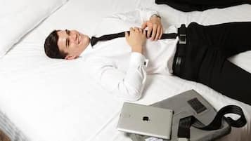 Uma pessoa deitada na cama com um laptop e um objeto preto ao lado.