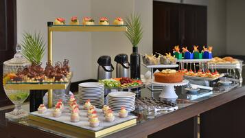 Mesa de buffet com diversos alimentos, incluindo cupcakes, frutas e um bolo.