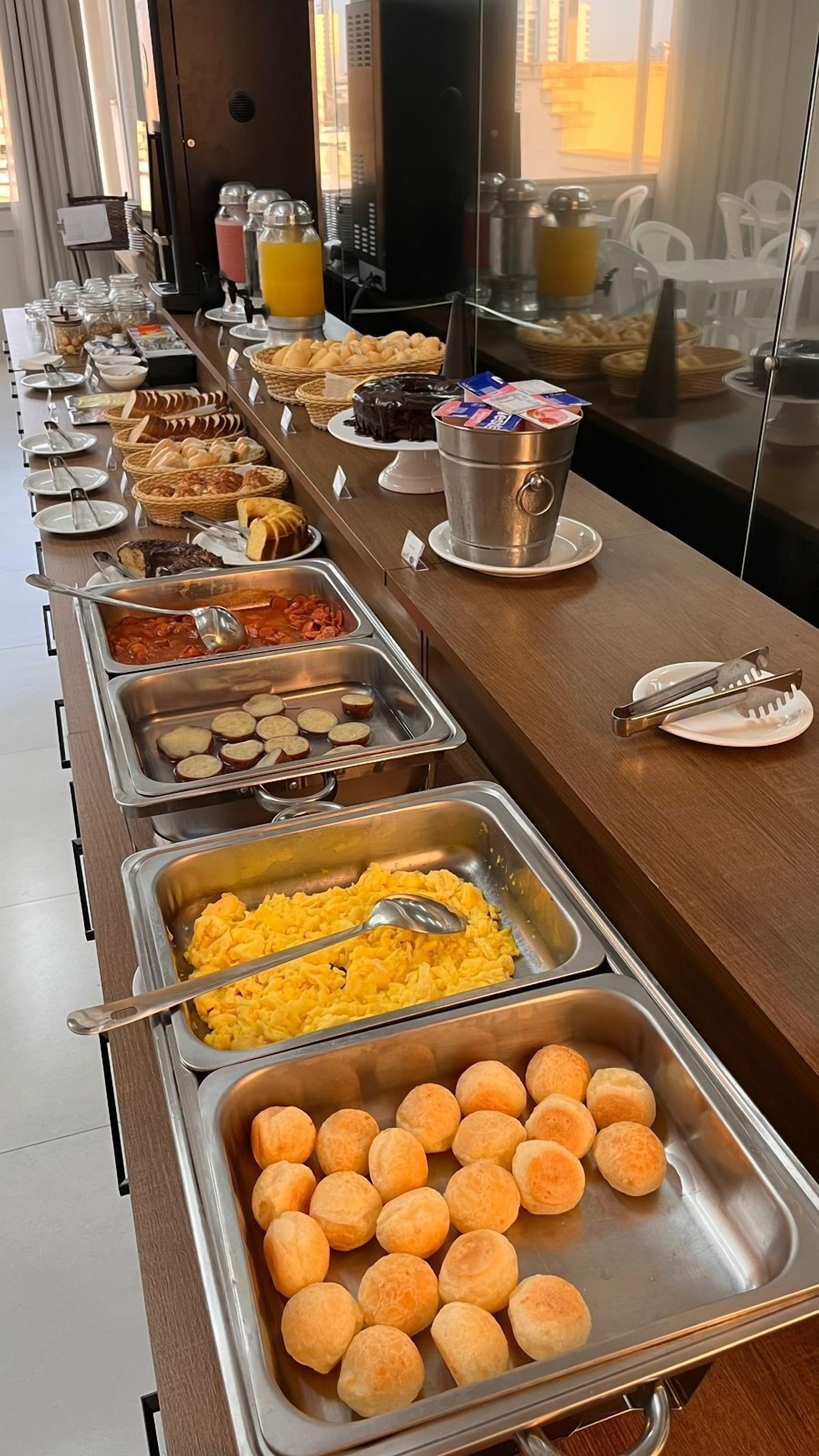 Buffet com diversas opções de comida, incluindo pão, ovos e doces.
