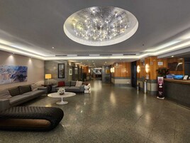 Um hall amplo com um lustre moderno, sofás, uma mesa de centro e um balcão de recepção.