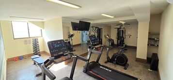 Uma academia com esteiras, aparelhos de musculação e um painel de espelhos.