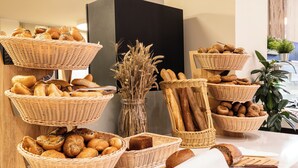 Uma mesa de buffet com diversos pães e doces em cestos de vime.
