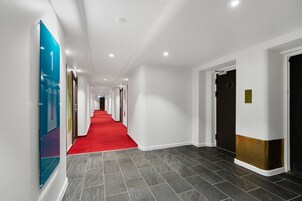 Corredor de hotel com tapete vermelho, paredes brancas e um sinal azul indicando números de quartos.