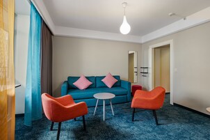 Quarto moderno com sofá azul, duas cadeiras laranja, uma mesa redonda pequena e um lustre.