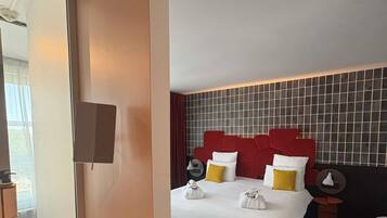 Quarto de hotel com cama, televisão na parede, mesa de cabeceira e janela.