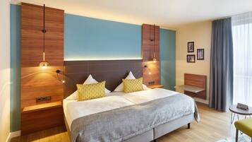 Quarto de hotel moderno com uma cama grande, duas mesas de cabeceira, uma mesinha de cabeceira menor, uma mesa redonda e uma cadeira.