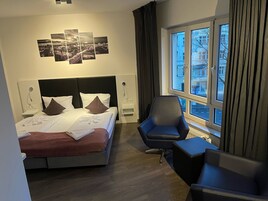 Quarto de hotel com cama, cadeira, janela e parede com fotografias.