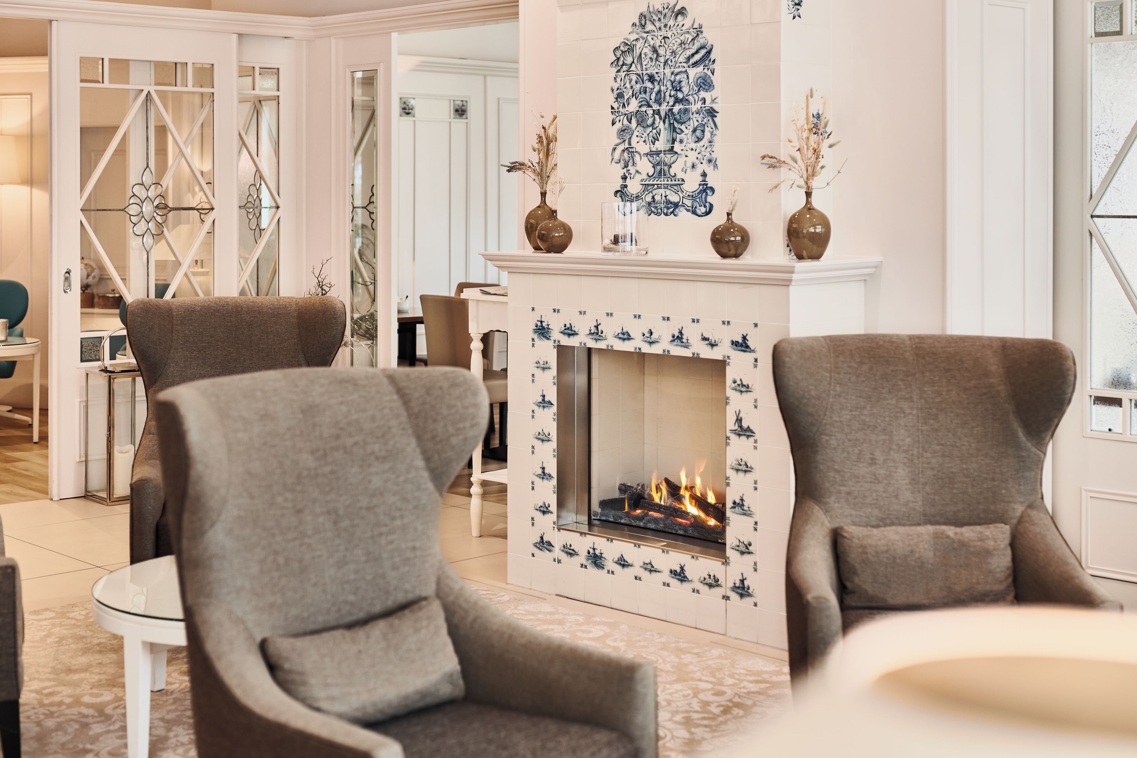 Uma sala de estar com dois poltronas, uma lareira com revestimento de azulejos e uma peça decorativa sobre a lareira.