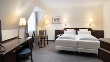 Quarto de hotel com cama, escrivaninha, cadeira e duas luminárias de cabeceira.