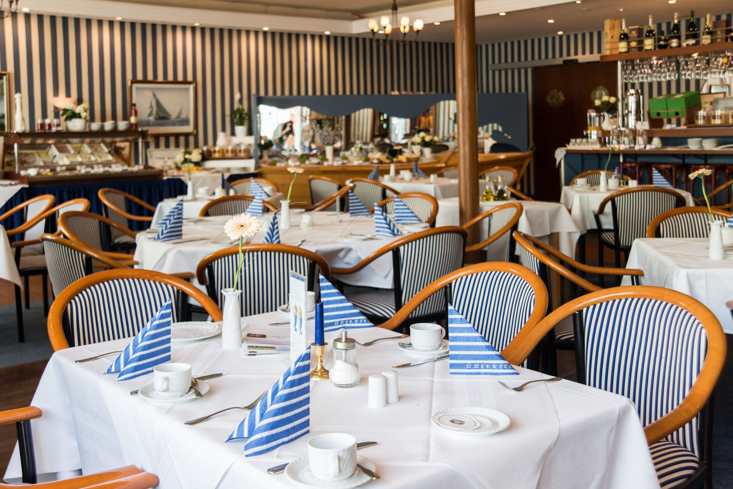 Um restaurante com cadeiras estofadas listradas, toalhas de mesa brancas e mesas de jantar bem arrumadas.
